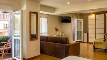 Quarto de hotel com cama, sofá marrom, televisão, porta de vidro deslizante e um divisor de ambientes tradicional japonês.