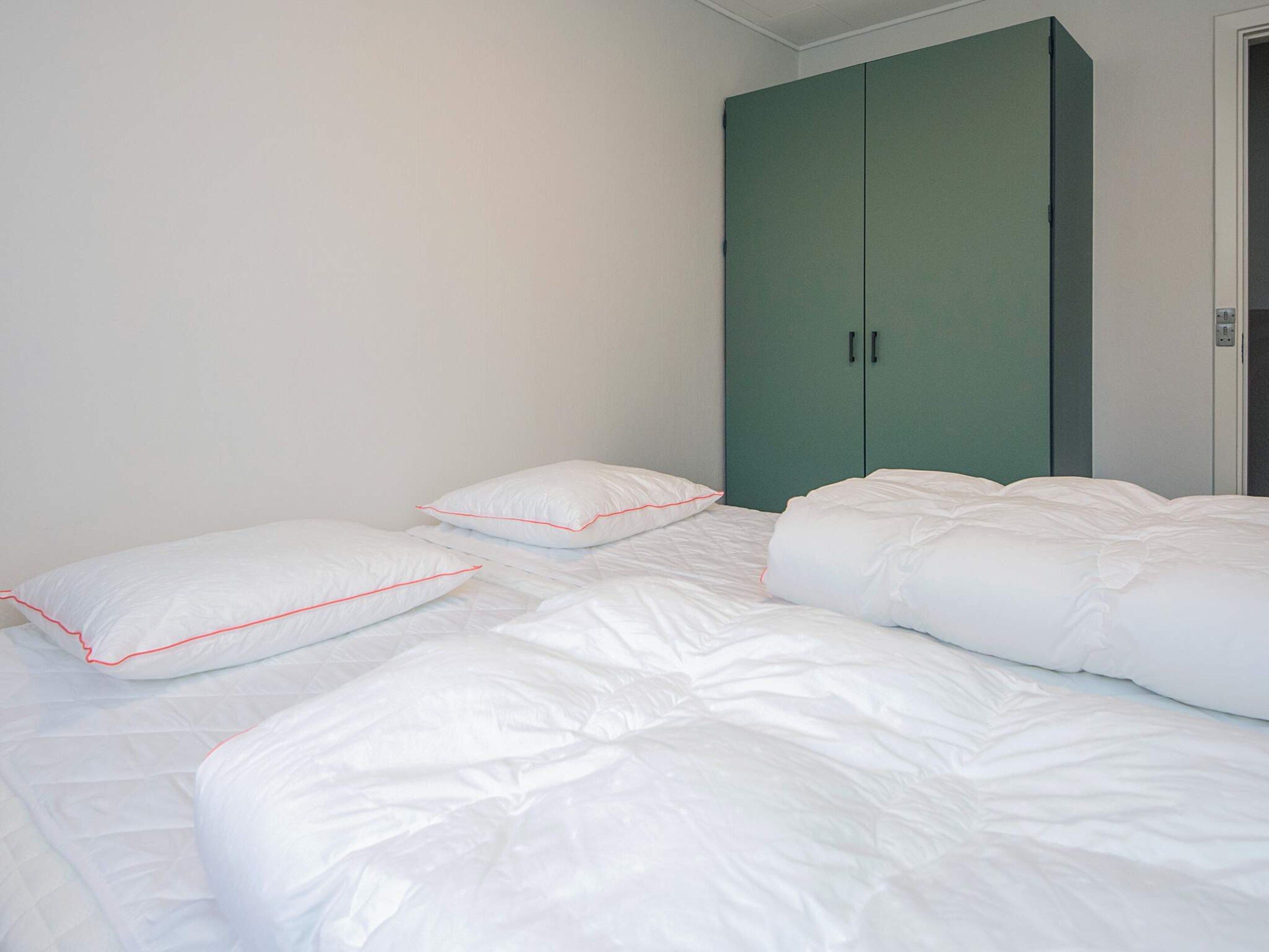 Quarto com cama, almofadas e um guarda-roupa verde.