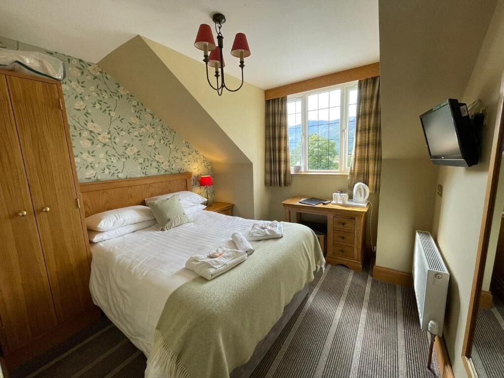 Quarto de hotel com cama, escrivaninha com computador, televisão e janela com cortinas.