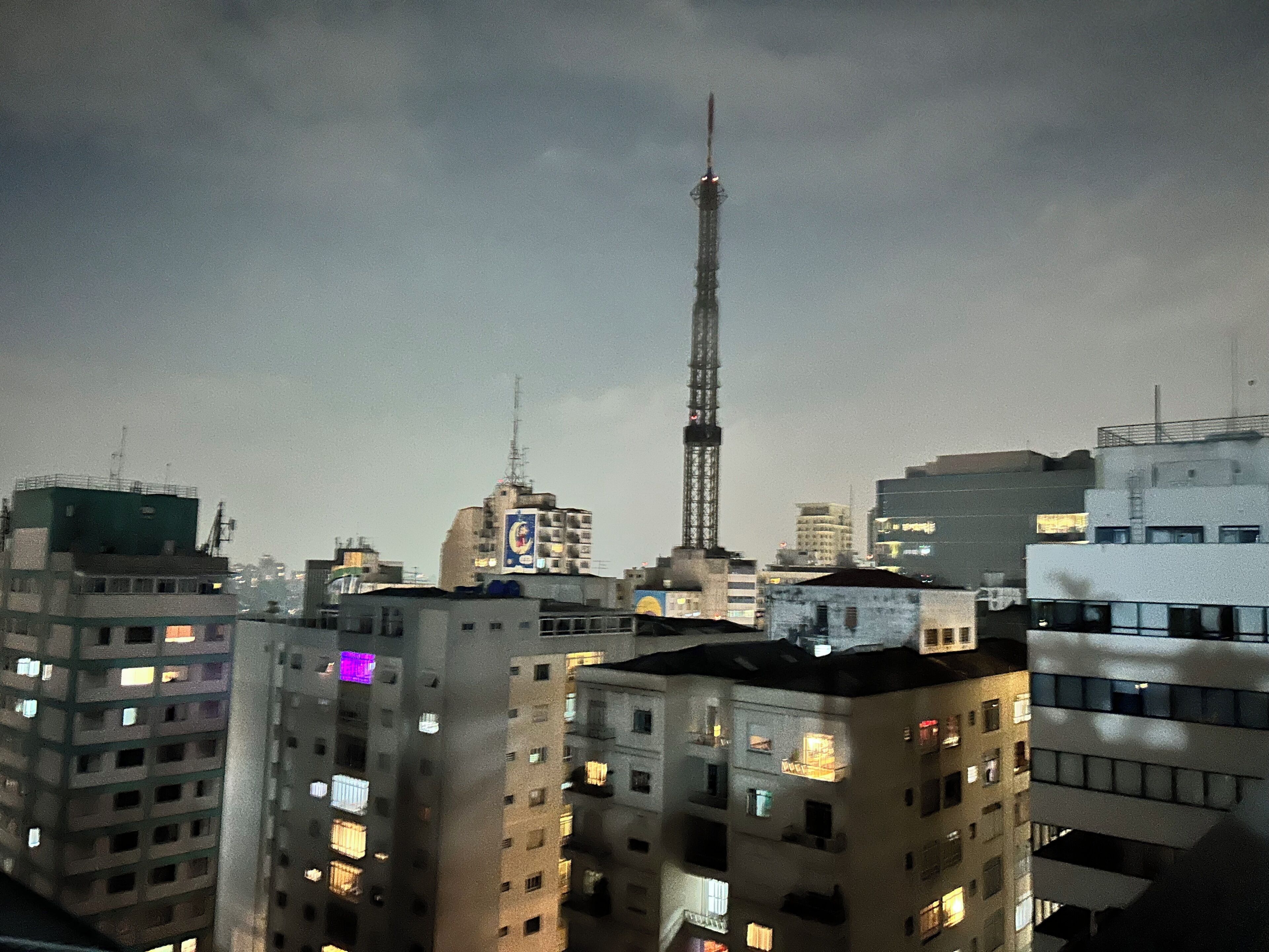 Um edifício alto com vários andares e varandas, cercado por outros edifícios.