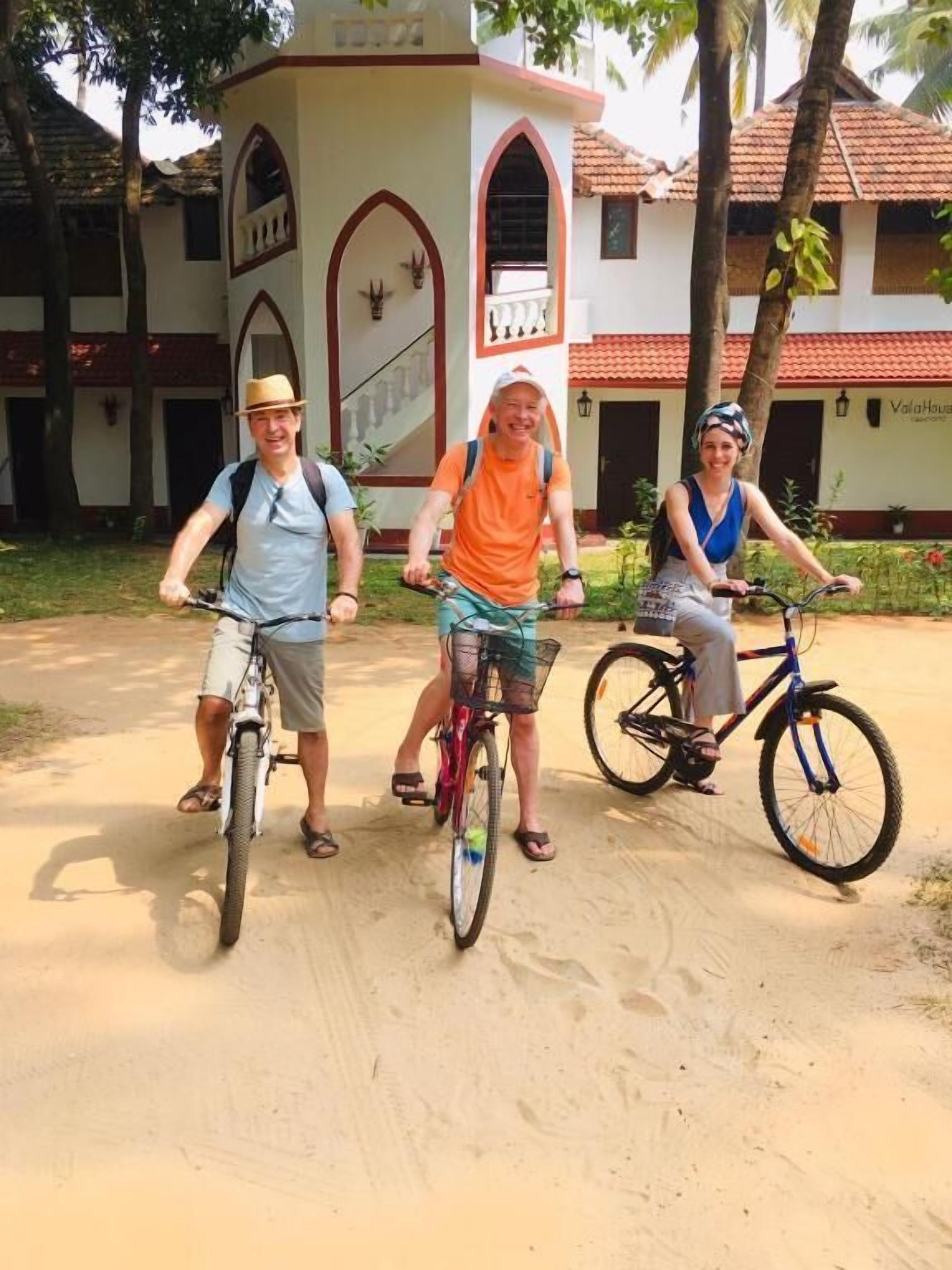 Três pessoas de bicicleta em frente a um edifício com torre do relógio.