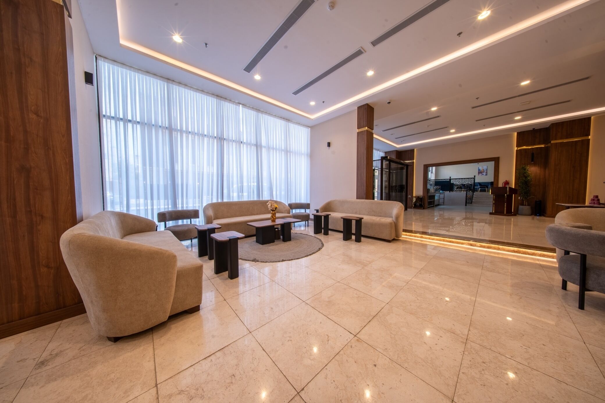 Um hall moderno com sofá, mesa de centro e cadeiras, janelas amplas e uma área de recepção.