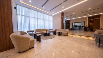 Um hall moderno com sofá, mesa de centro e cadeiras, janelas amplas e uma área de recepção.