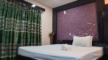 Uma cama bem arrumada com lençóis brancos e uma toalha dobrada, parede roxa com textura e cortina verde com padrão.
