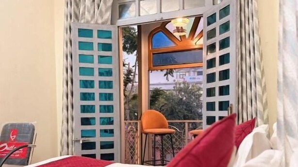 Quarto de hotel com cama, almofada vermelha, cadeira e janela com cortinas.