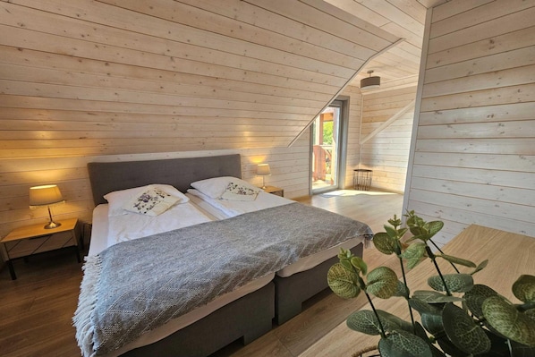 Quarto com cama, luminárias de cabeceira, janela e escada para um andar superior.