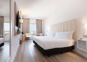 Quarto de hotel com uma cama grande, uma televisão na parede, uma mesinha e uma cadeira.