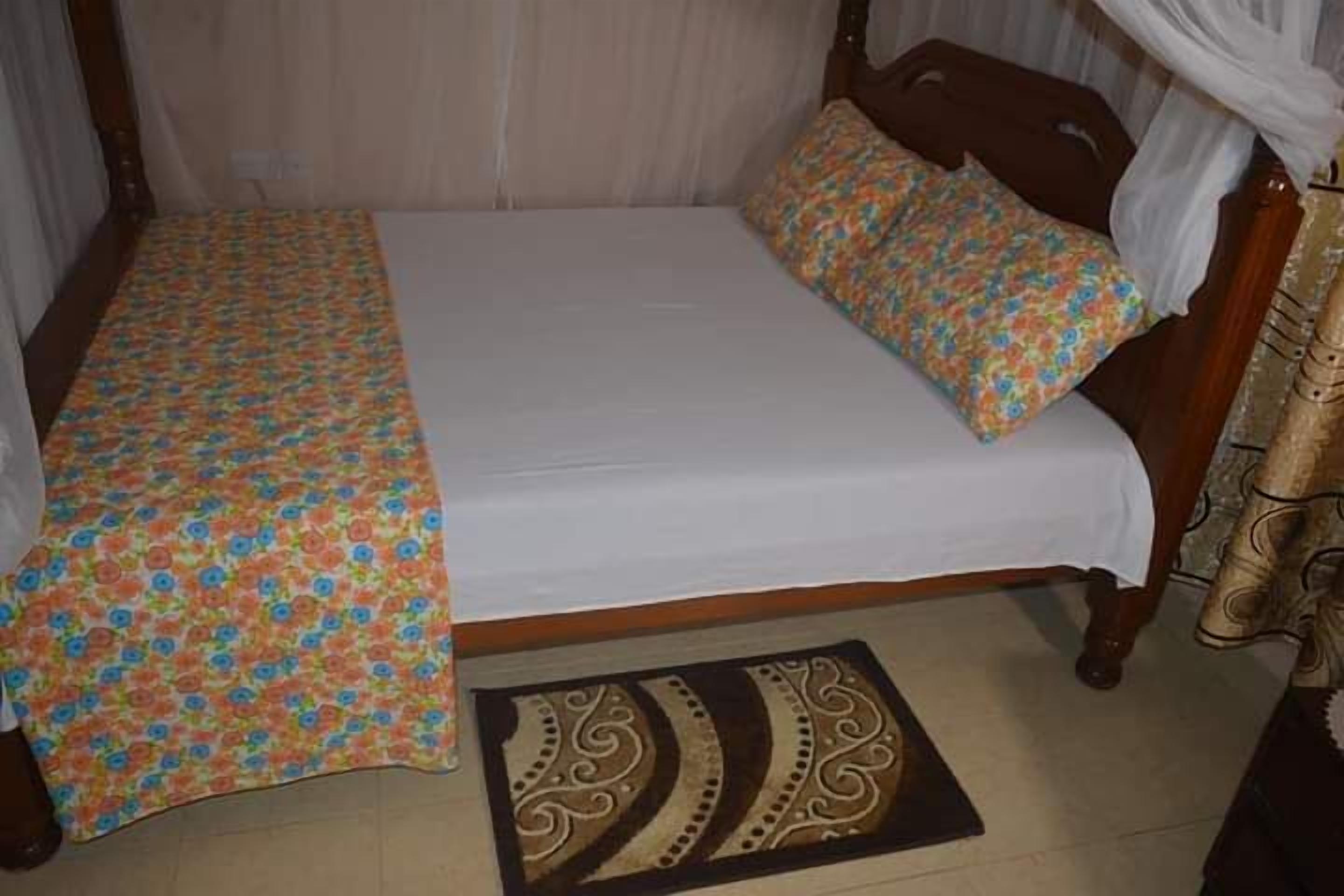 Uma cama de solteiro com colcha floral, almofada combinando e um tapete decorativo.