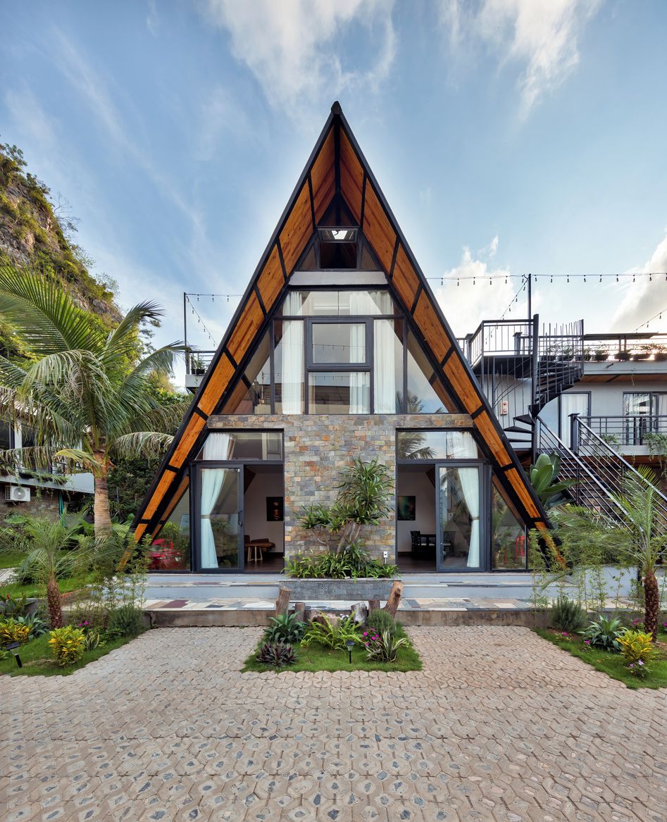 Uma casa moderna com telhado triangular, janelas amplas e entrada pavimentada.