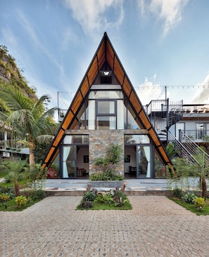 Uma casa moderna com telhado triangular, janelas amplas e entrada pavimentada.