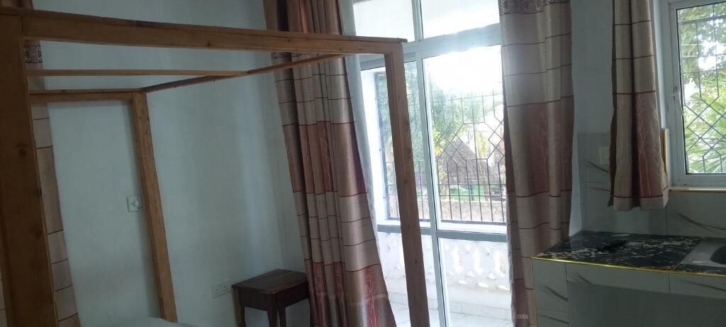 Quarto com estrutura de madeira, um banquinho pequeno e janela com cortinas.