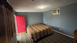 Quarto com uma cama, uma porta vermelha, uma luminária no teto e um aparelho de ar condicionado.