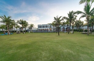 Um hotel com um amplo gramado, palmeiras e um edifício com janelas em arco.