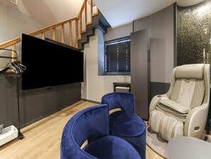 Uma sala de estar moderna com televisão de tela plana, uma poltrona azul, uma cadeira de massagem e uma escada.