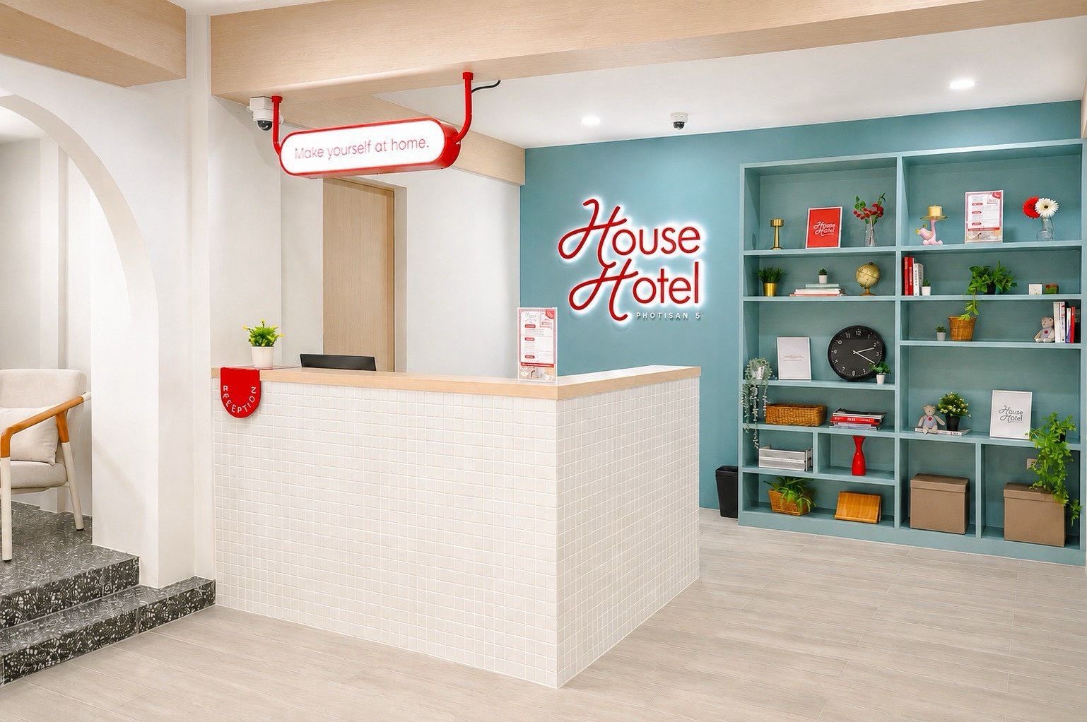 Uma área de recepção de hotel com balcão, placa na parede e estante com diversos objetos.
