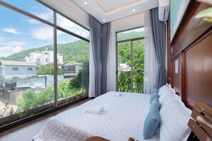 Quarto de hotel com uma cama grande, cabeceira de madeira e vista para a cidade e áreas verdes.