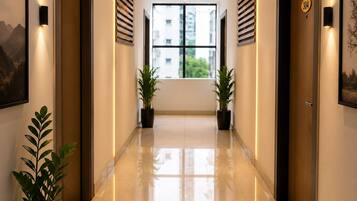 Corredor de hotel com piso lustroso, plantas em vasos e portas com placa de identificação.