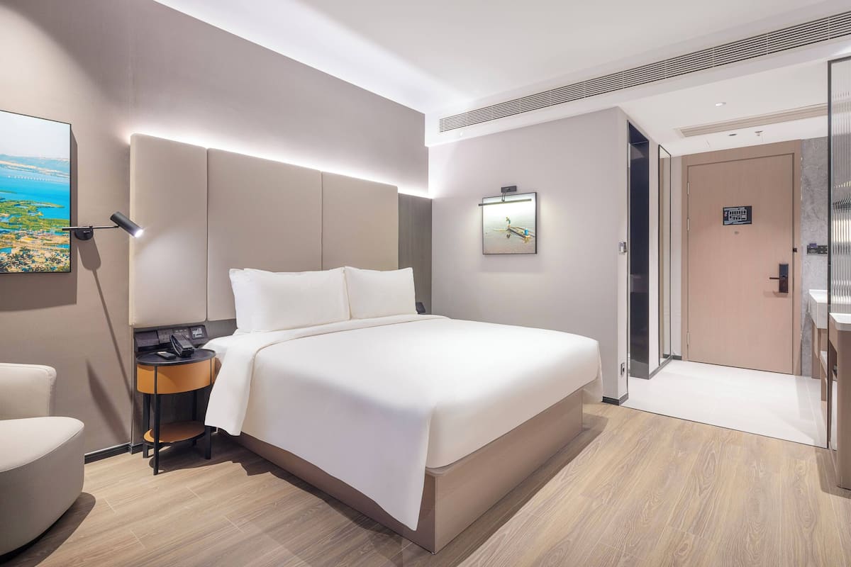 Quarto de hotel moderno com cama grande, mesa de cabeceira, luminária e um quadro na parede.