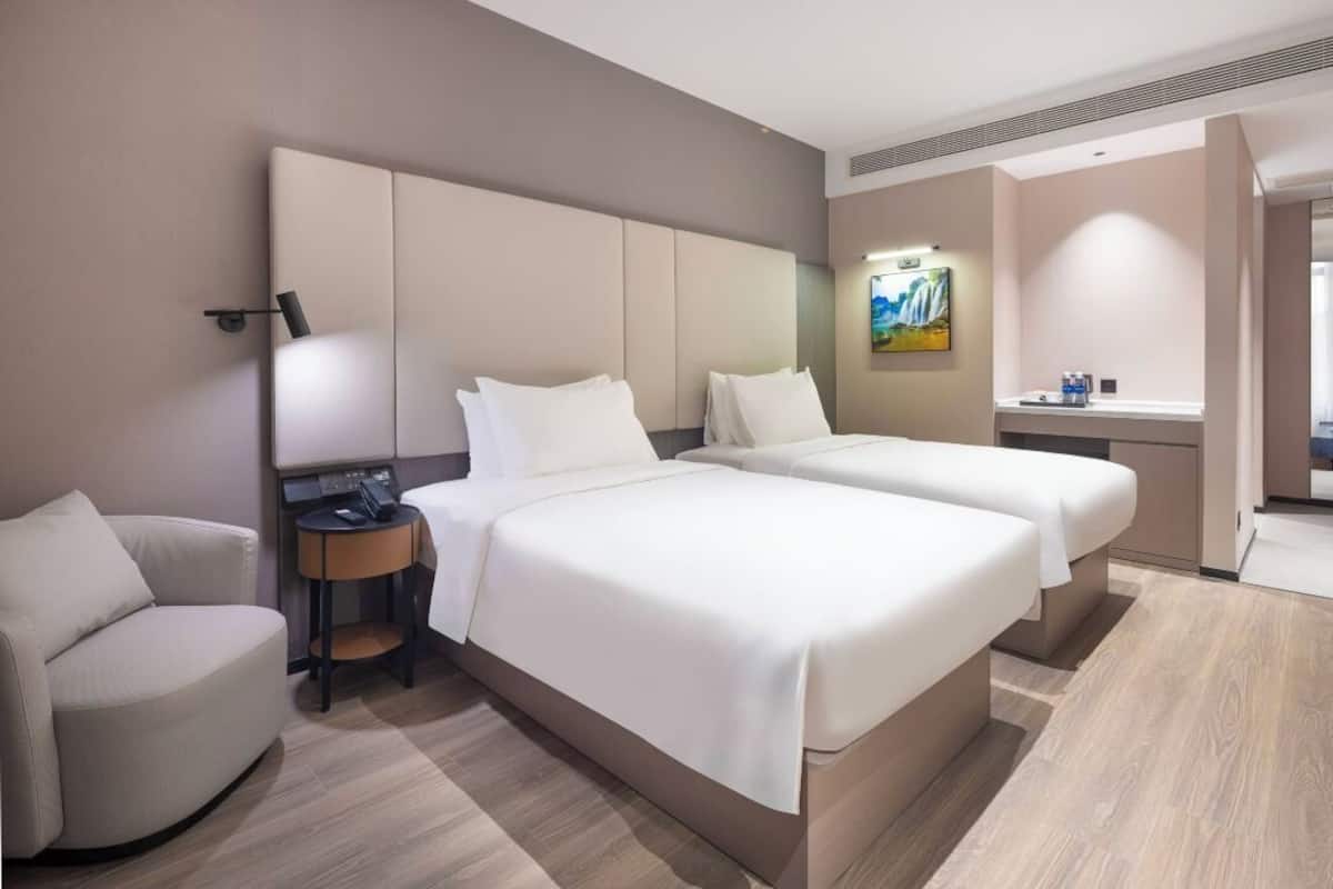 Quarto de hotel com duas camas, uma escrivaninha, uma cadeira e um quadro na parede.