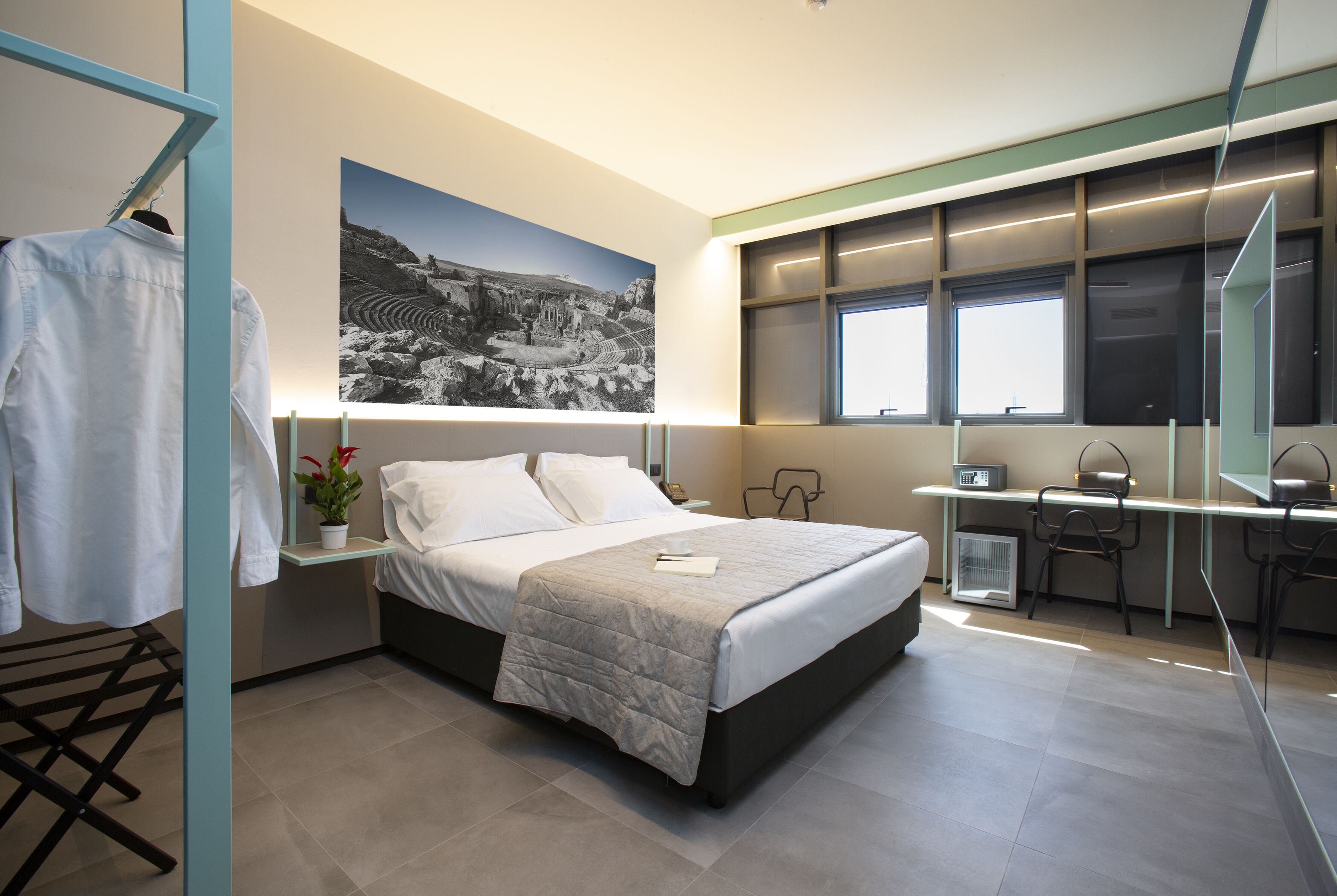 Quarto de hotel moderno com uma cama grande, uma escrivaninha e vista para uma paisagem montanhosa.