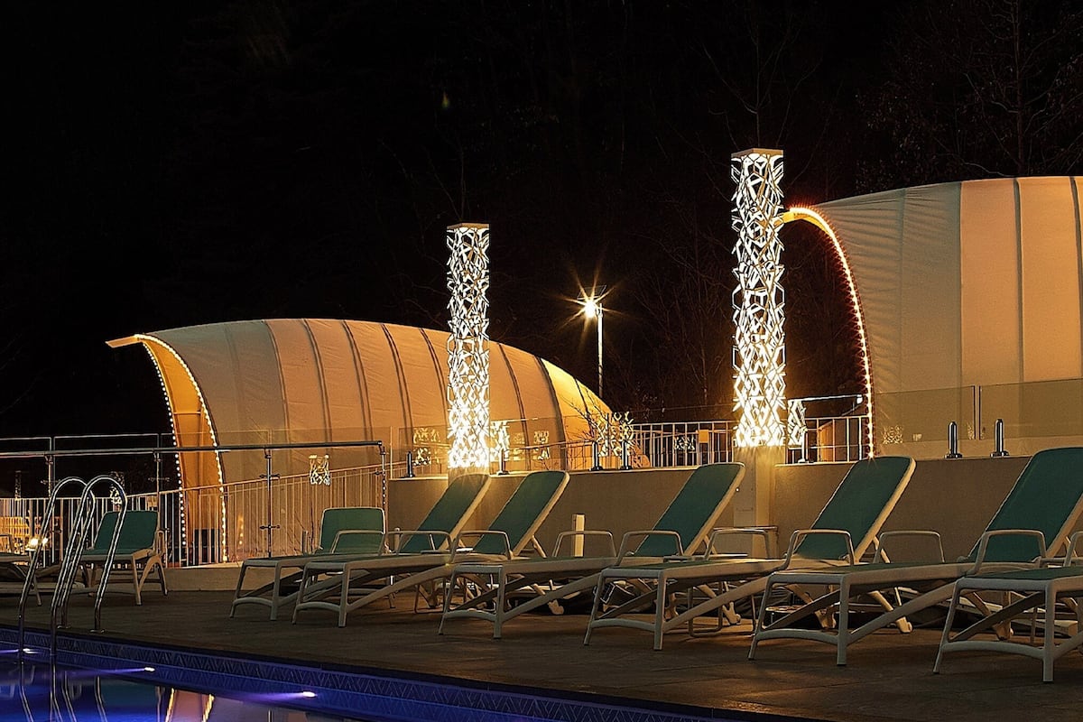 Uma área à beira da piscina com espreguiçadeiras e um espaço coberto para sentar, refletindo na água.