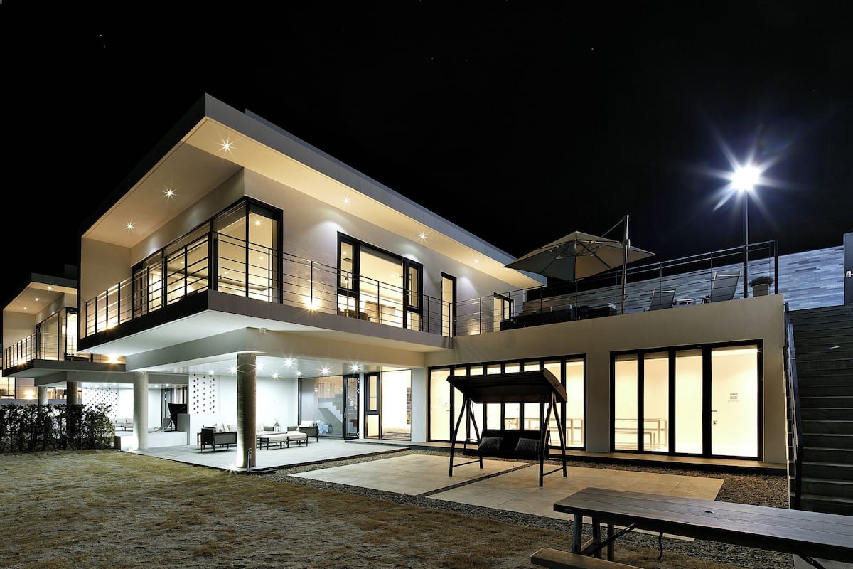 Uma casa moderna de dois andares com um amplo pátio, janelas grandes e área coberta para sentar.