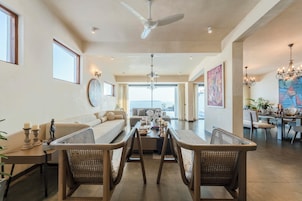 Uma sala de estar ampla com teto alto, uma mesa de jantar com cadeiras e vista para o exterior.