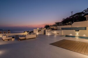 Terraço no telhado com área de estar externa, piscina e vista para o mar ao anoitecer.
