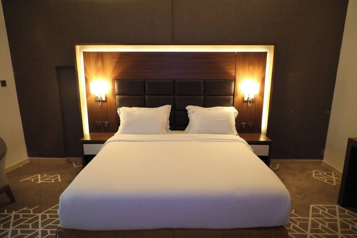 Uma cama grande com cabeceira, duas mesas de cabeceira e luminárias fixadas na parede.