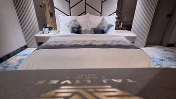 Quarto de hotel moderno com uma cama grande, uma televisão de tela plana acima dela e uma cabeceira decorativa.