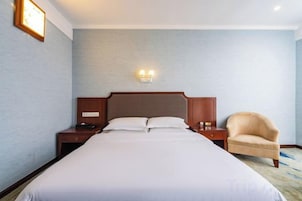 Quarto de hotel com uma cama grande, duas mesas de cabeceira, uma cadeira e luminária fixada na parede.