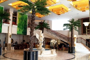 Um saguão com palmeira, estátua, escadaria e balcão de recepção.