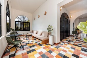 Um quarto com piso xadrez, um sofá, uma mesa de jantar com cadeiras e uma janela grande.