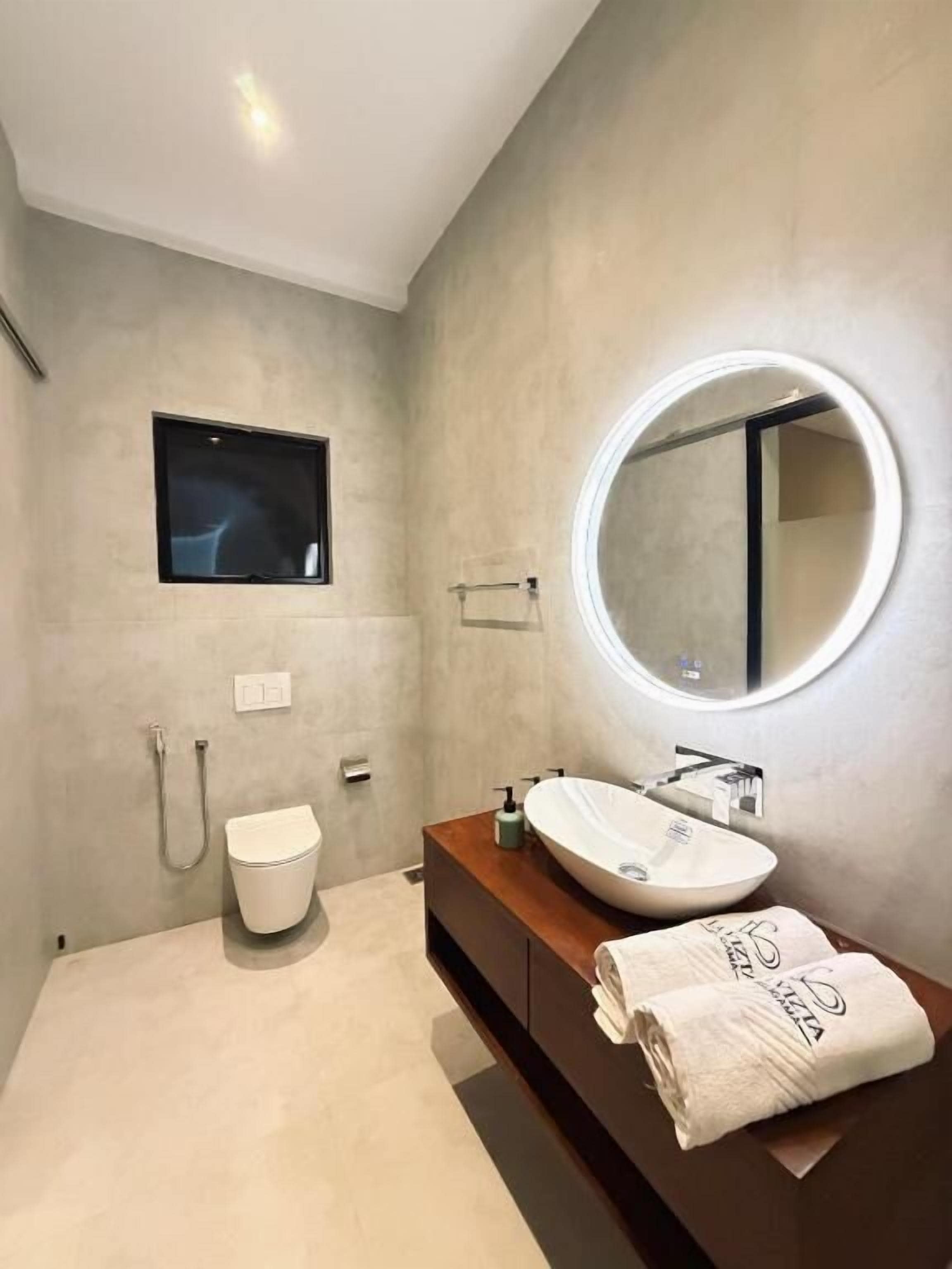 Uma casa de banho moderna com um espelho redondo grande, uma pia branca e um toucador de madeira.
