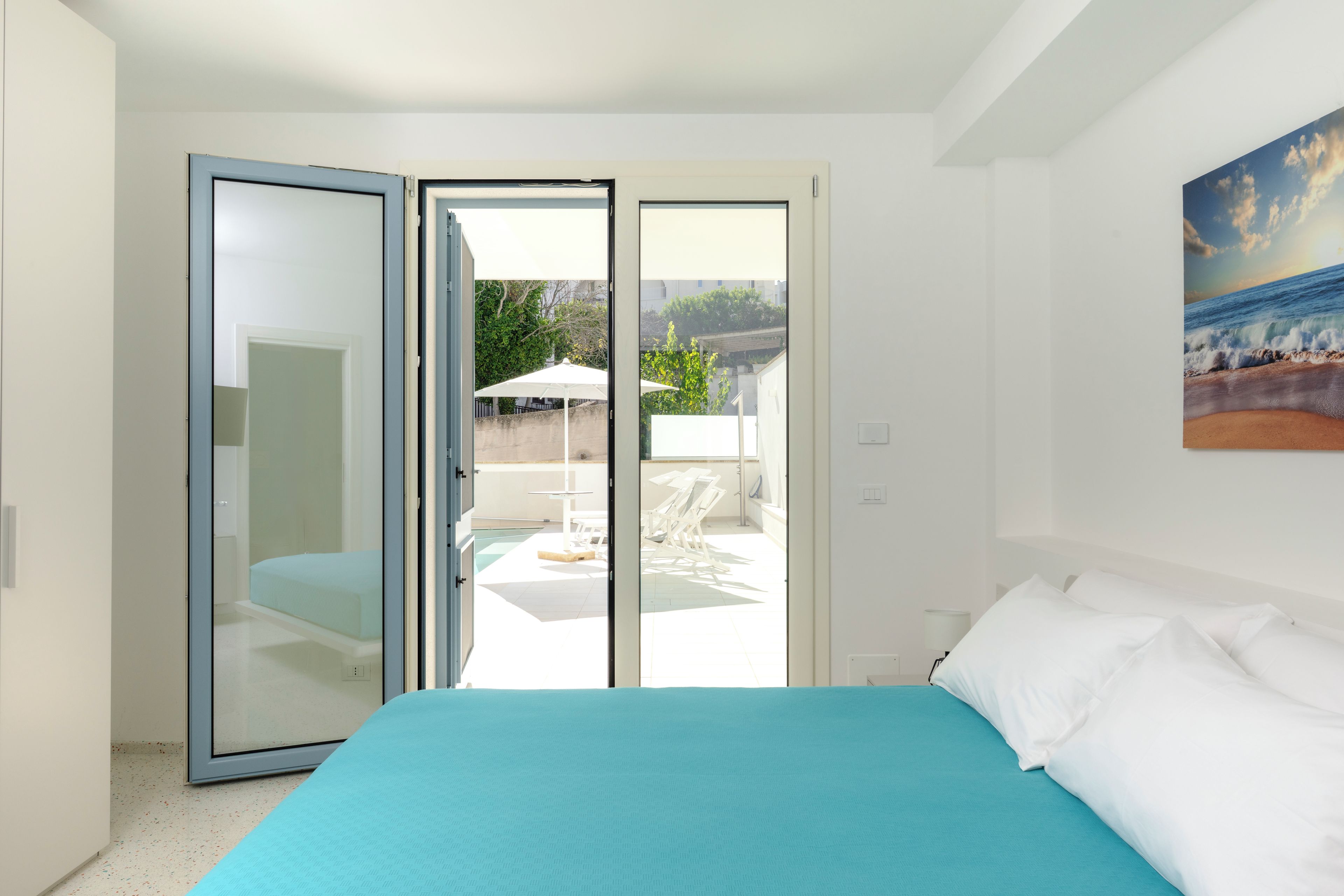 Quarto com cama, porta de vidro deslizante para uma varanda e um quadro na parede.