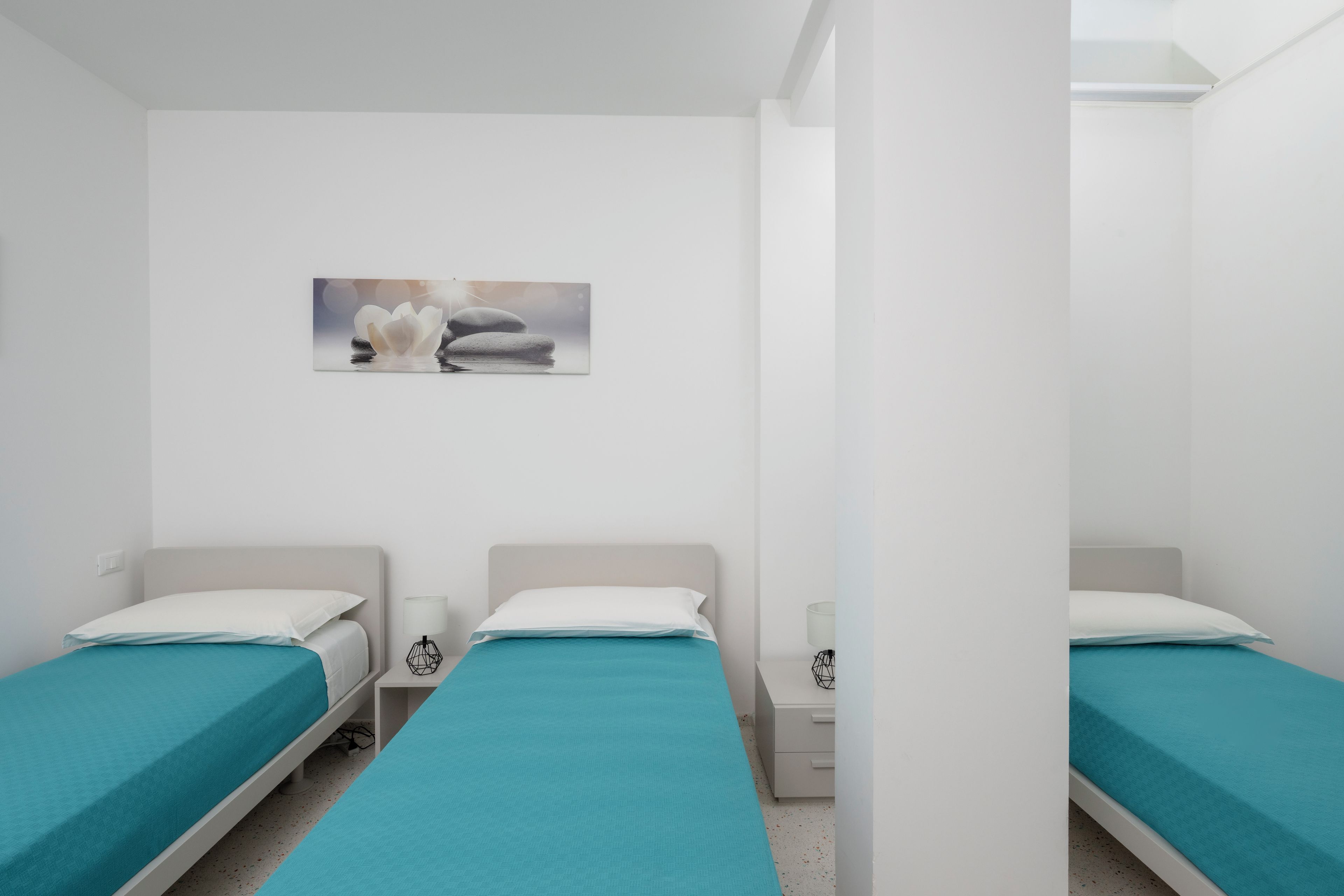 Quarto de hotel com duas camas de solteiro, mesa de cabeceira com luminária e um quadro pendurado na parede.