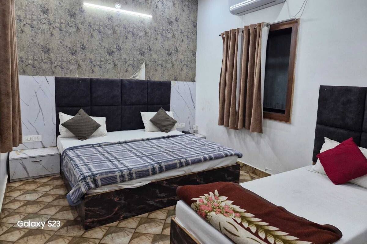 Quarto com uma cama grande, uma cama menor, uma mesa de cabeceira, um aparelho de ar condicionado e uma janela com cortinas.