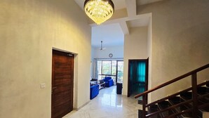 Um corredor amplo com piso de mármore, porta de madeira, escada e um lustre moderno.