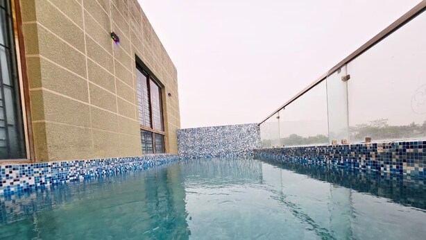 Uma piscina com água azul cristalina, paredes azulejadas e guarda-corpo de vidro.