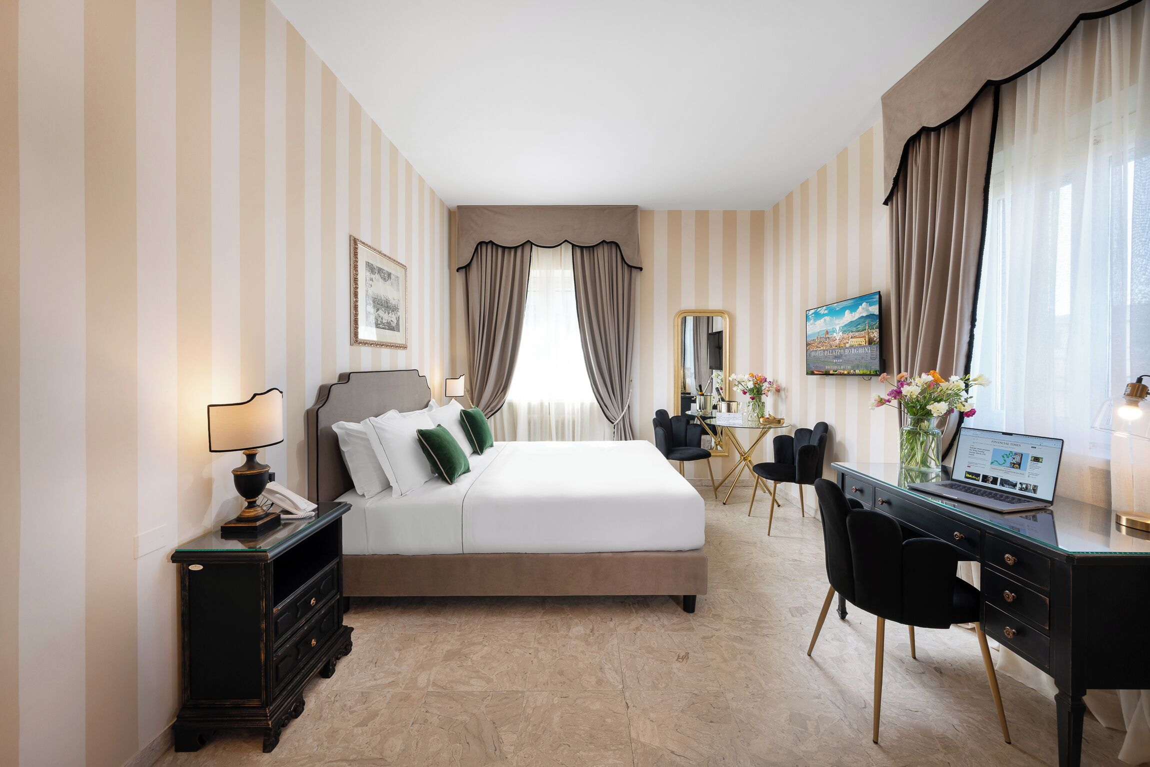Quarto de hotel com cama, mesa de cabeceira, escrivaninha, cadeira e um laptop.