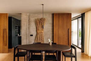 Uma sala de jantar moderna com uma mesa redonda, cadeiras pretas, um lustre e uma grande janela com cortinas.