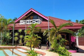 Um edifício de dois andares com telhado de telhas vermelhas, varanda e piscina.