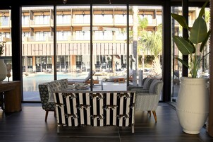 Interior moderno com sofá, grandes janelas e vista para uma piscina e um edifício.
