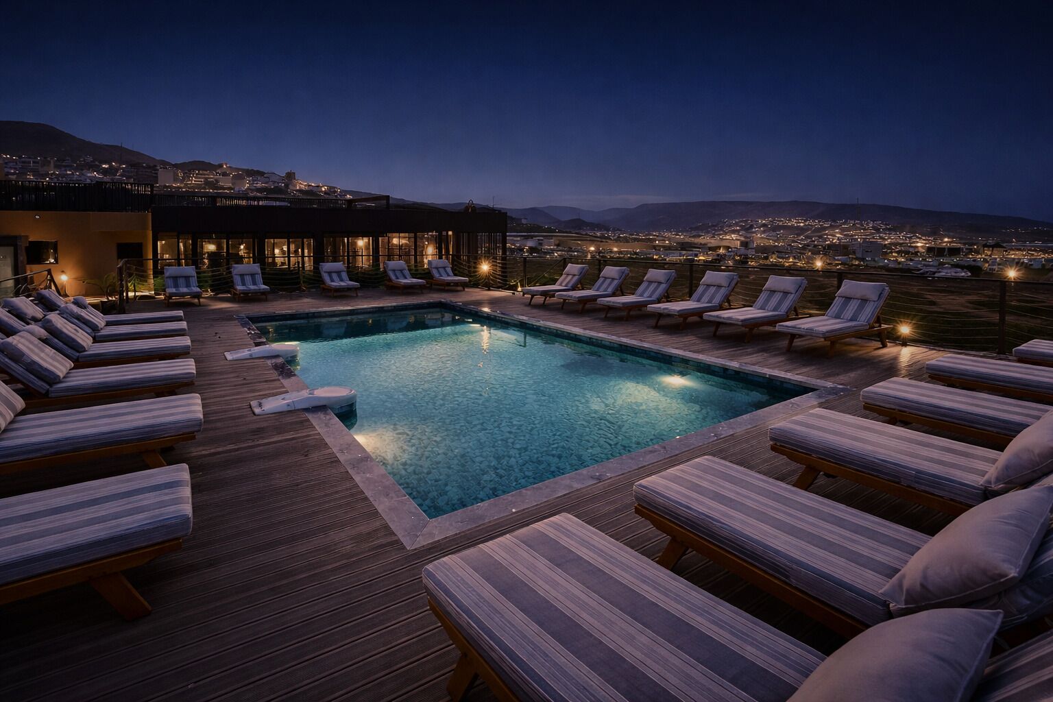 Uma área de piscina com espreguiçadeiras e vista para a paisagem urbana ao entardecer.
