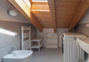 Casa de banho compacta com lavatório, porta-toalhas, prateleira e máquina de lavar roupa.
