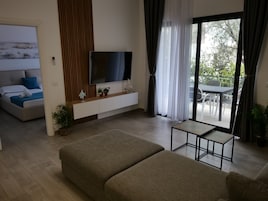 Uma sala de estar moderna com sofá, televisão presa a um painel de madeira, uma mesa pequena e uma varanda com mobiliário de exterior.