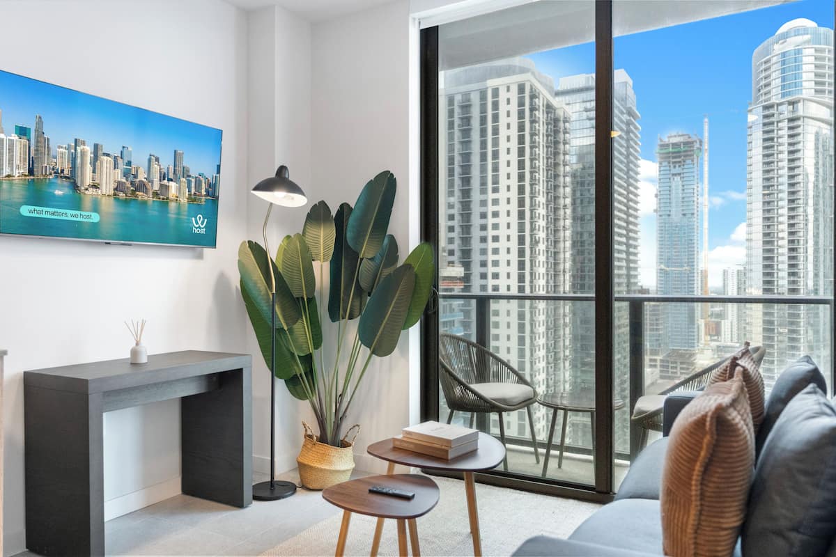 Uma sala de estar moderna com vista para a cidade, uma planta grande, um sofá, uma mesa pequena e um aparador.