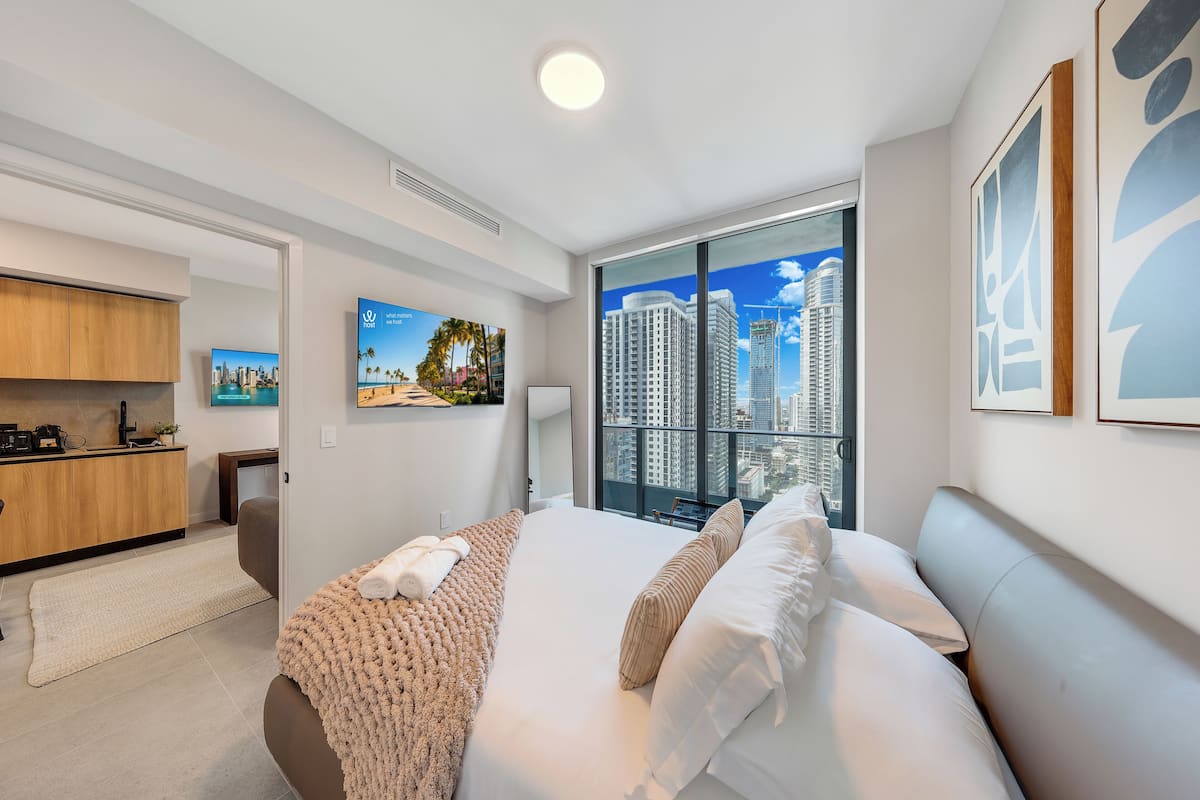 Quarto de hotel moderno com uma cama grande, uma escrivaninha e vista para edifícios altos.
