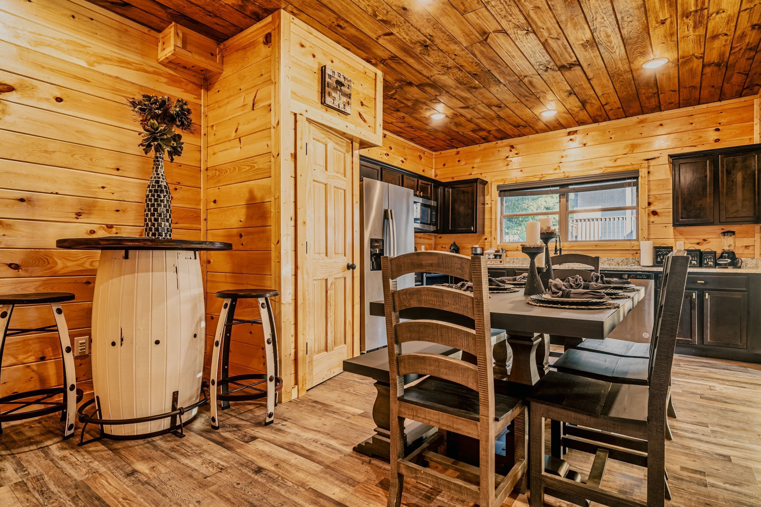 Interior de uma cabana de madeira com sala de jantar, cozinha e um relógio na parede.