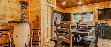 Interior de uma cabana de madeira com sala de jantar, cozinha e um relógio na parede.